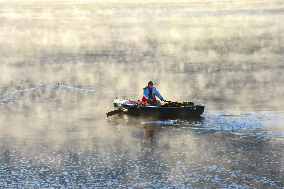 Ang mangingisda ay naglayag sa isang bangka sa pamamagitan ng tabing ng umaga sa isang titisa lake sa Black Forest, Germany.